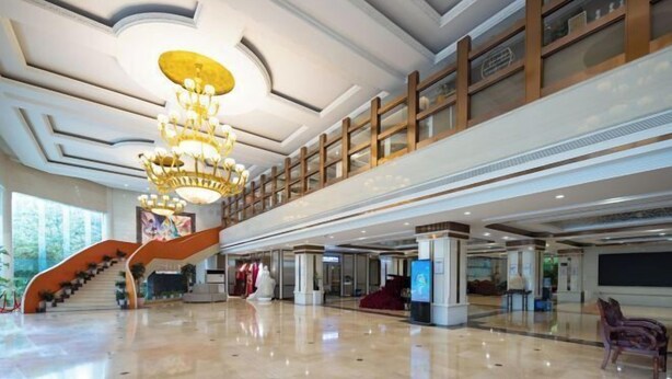 Um hall espaçoso com um lustre imponente, uma escadaria e um corrimão de vidro com vista para o nível inferior.