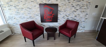 Um quarto com duas cadeiras vermelhas, uma mesa redonda pequena e o letreiro 'Red Roof Inn' na parede.