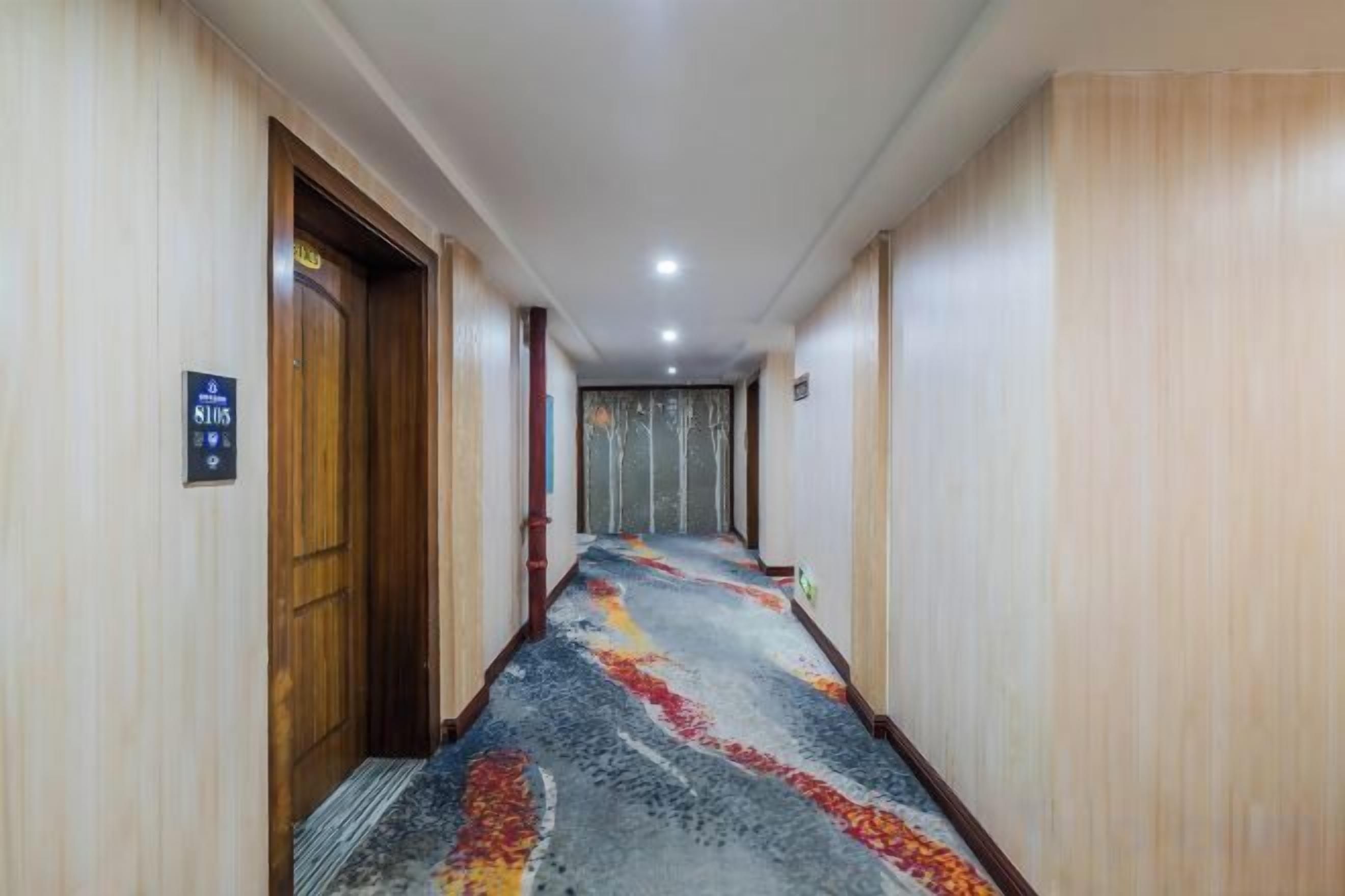 Corredor de hotel com piso carpetado, portas de madeira e uma placa indicando a direção do elevador.