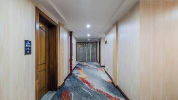 Corredor de hotel com piso carpetado, portas de madeira e uma placa indicando a direção do elevador.