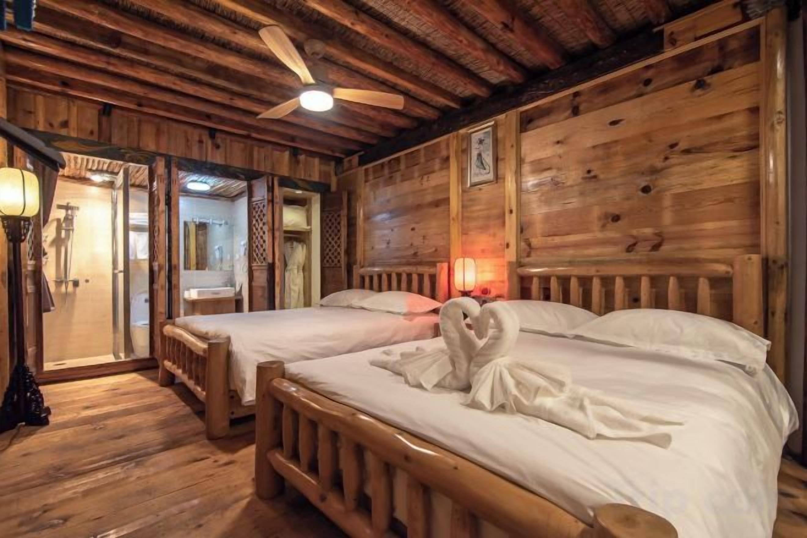 Quarto rústico estilo cabana com duas camas, um ventilador de teto e porta para o banheiro.