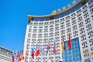 Um hotel com várias andares e fachada curva, com inúmeras janelas e bandeiras de diversos países exibidas na parte externa.