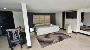 Quarto moderno com cama, televisão, espelho e uma pequena mesa.