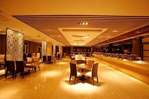 Um amplo hall de hotel com área de estar central, um balcão de recepção longo e um design de teto moderno.