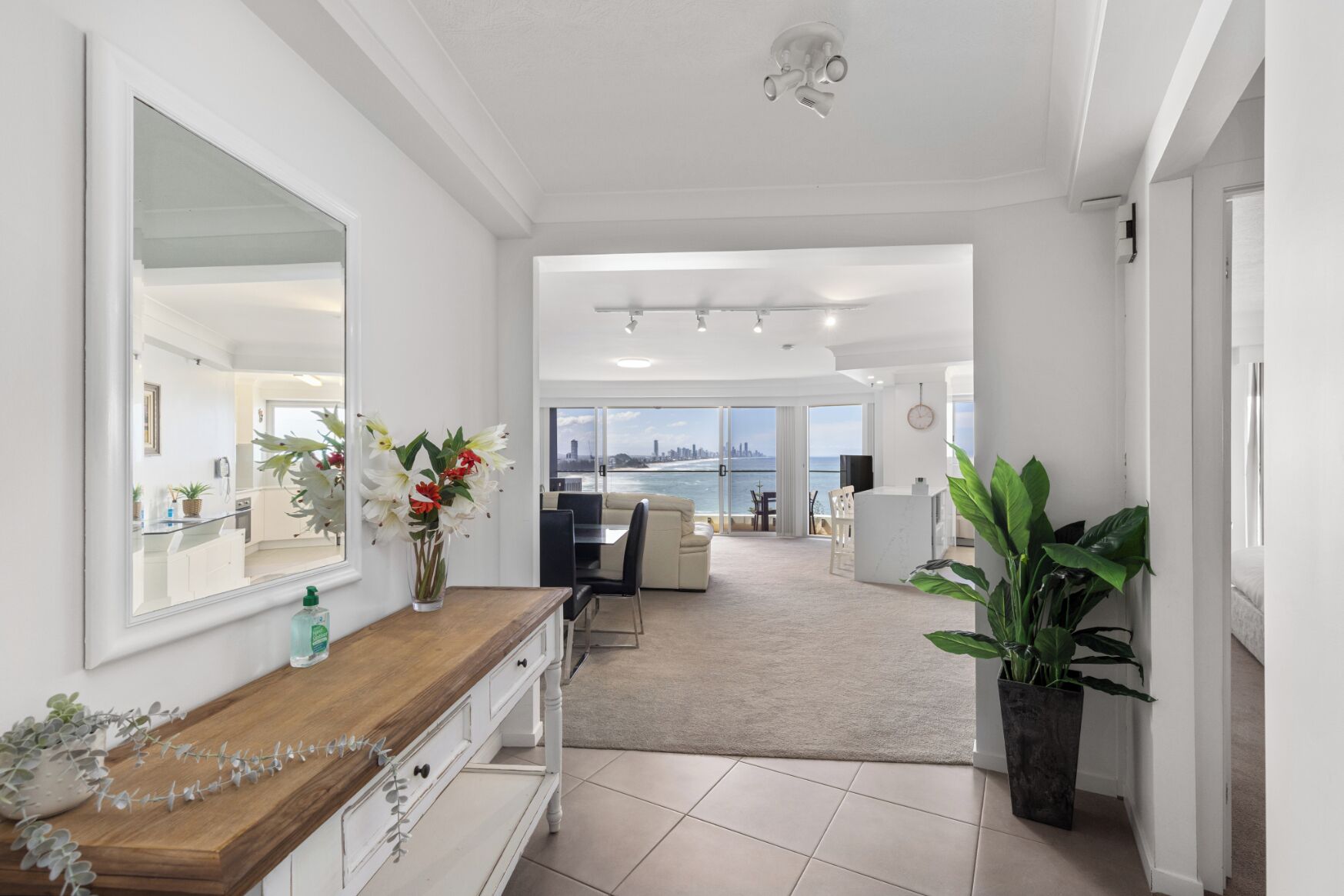 Um corredor amplo com vista para o horizonte da cidade e do oceano, que dá acesso a uma sala de jantar com mesa e cadeiras.