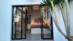 Quarto com cama, mesa de cabeceira e uma janela grande.