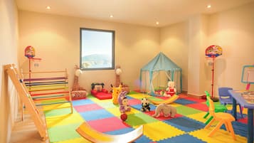 Uma sala de jogos infantil com escorrega, tapetes de atividades e diversos brinquedos.