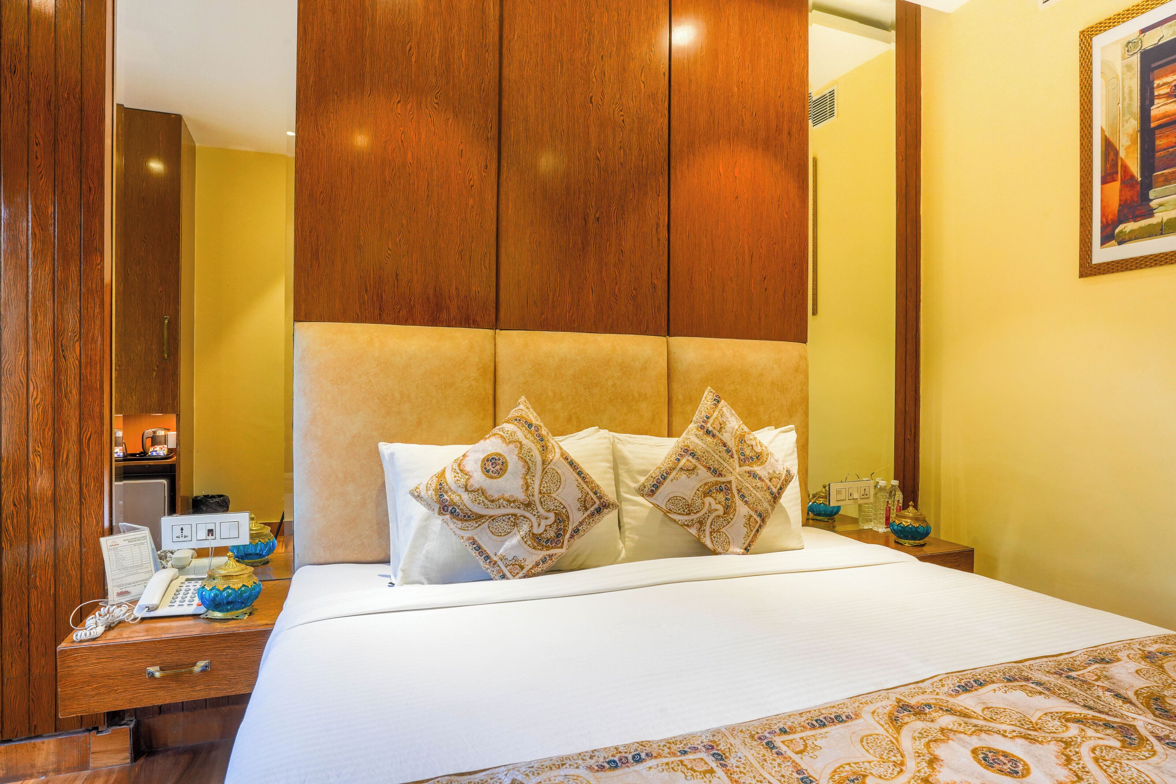 Quarto de hotel com cama grande, cabeceira de madeira e mesa de cabeceira com abajur e telefone.