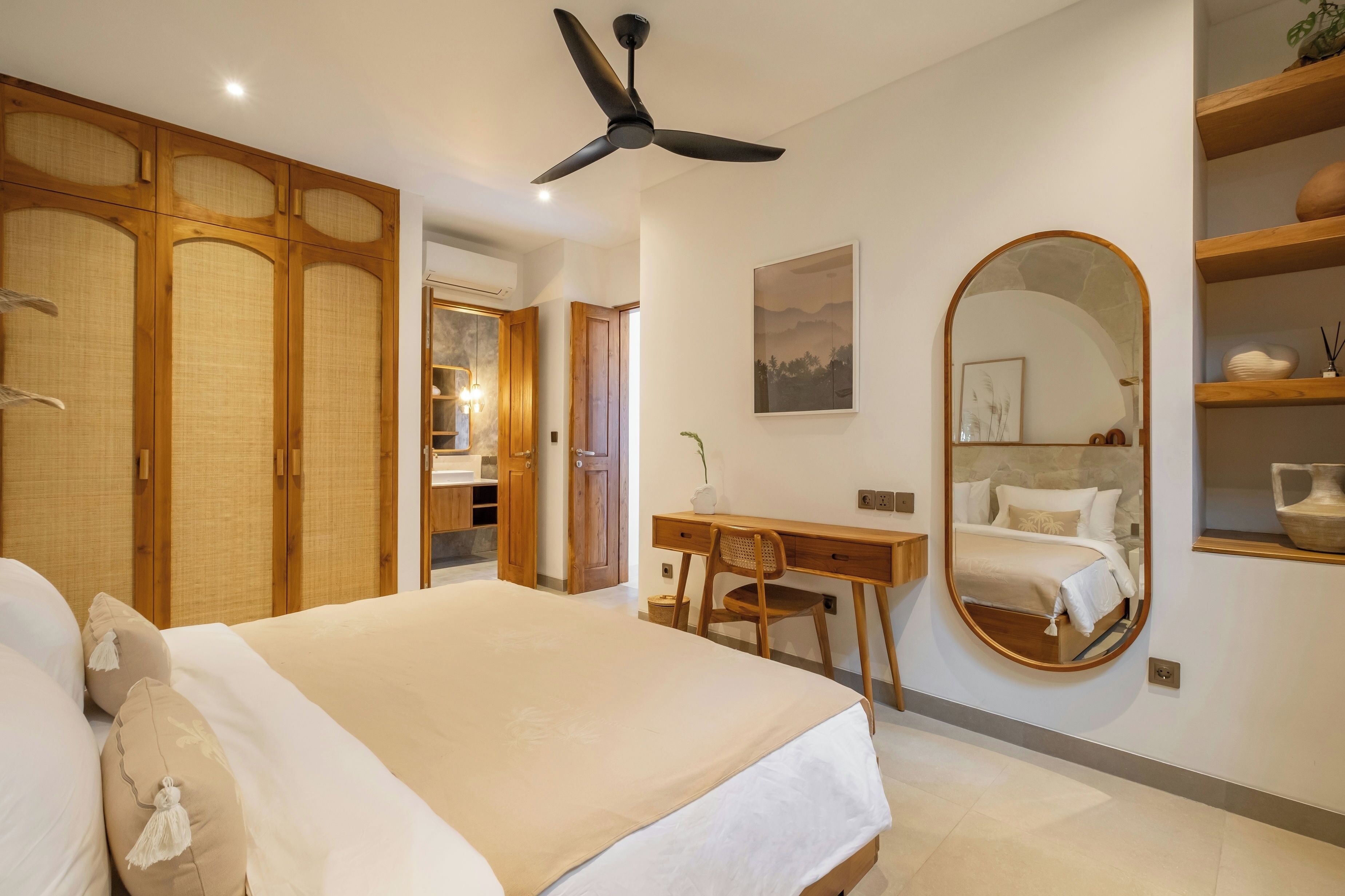 Quarto com cama, escrivaninha, cadeira, ventilador de teto, espelho e guarda-roupa.