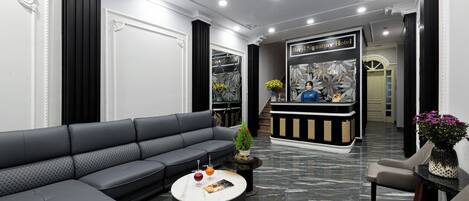 Um hall de hotel moderno com um sofá de couro preto, uma mesa de centro de mármore e uma mesa de recepção.