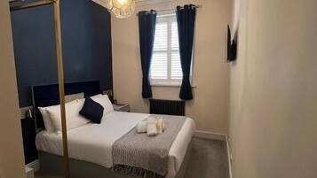 Um quarto com cama, mesa de cabeceira, espelho, janela com cortinas e luminária no teto.