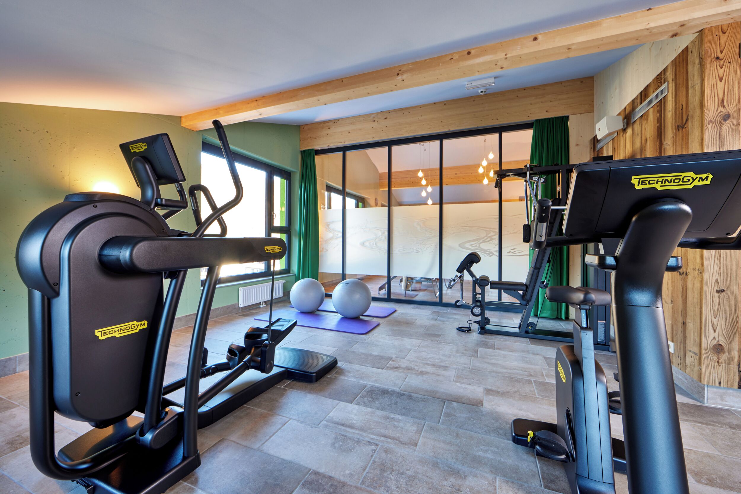 Uma academia com equipamentos de cardio, tapete de yoga e bolas de exercícios.