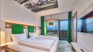 Quarto de hotel com cama, escrivaninha, cadeira e vista para montanhas pela janela.
