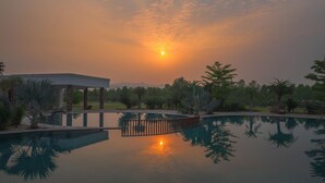 Área de piscina tranquila com um gazebo, cercada por palmeiras e um céu claro.