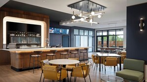 Uma área de bar moderna com balcão, banquetas e um espaço de estar com mesas redondas e cadeiras.