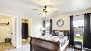 Quarto com cama de madeira, ventoinha no teto, janela com cortinas e vista para o exterior.
