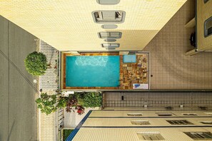 Vista aérea de um edifício com piscina, área de varanda coberta e calçada de azulejos.