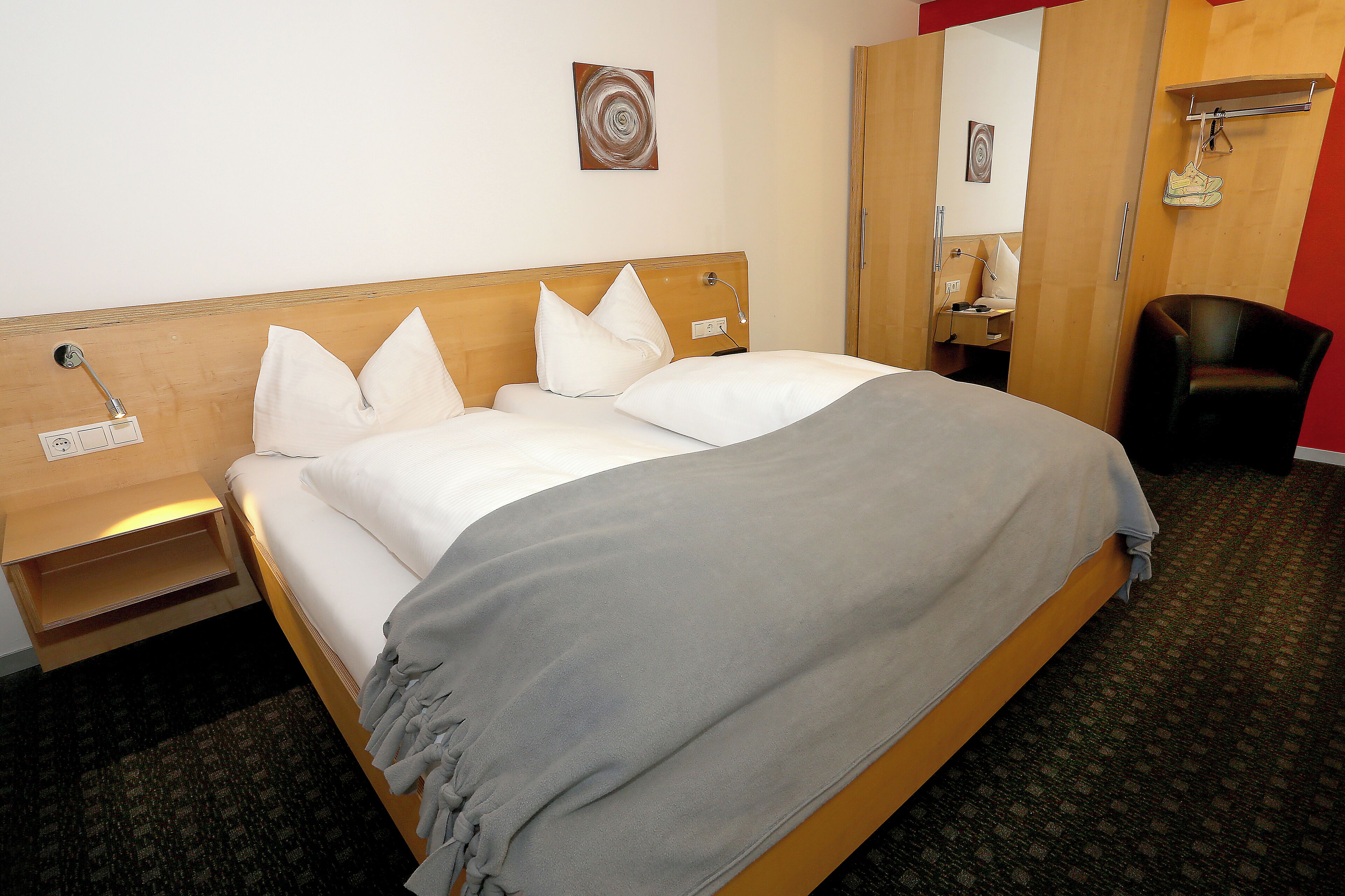 Quarto de hotel com cama, mesa de cabeceira, cadeira e guarda-roupa.