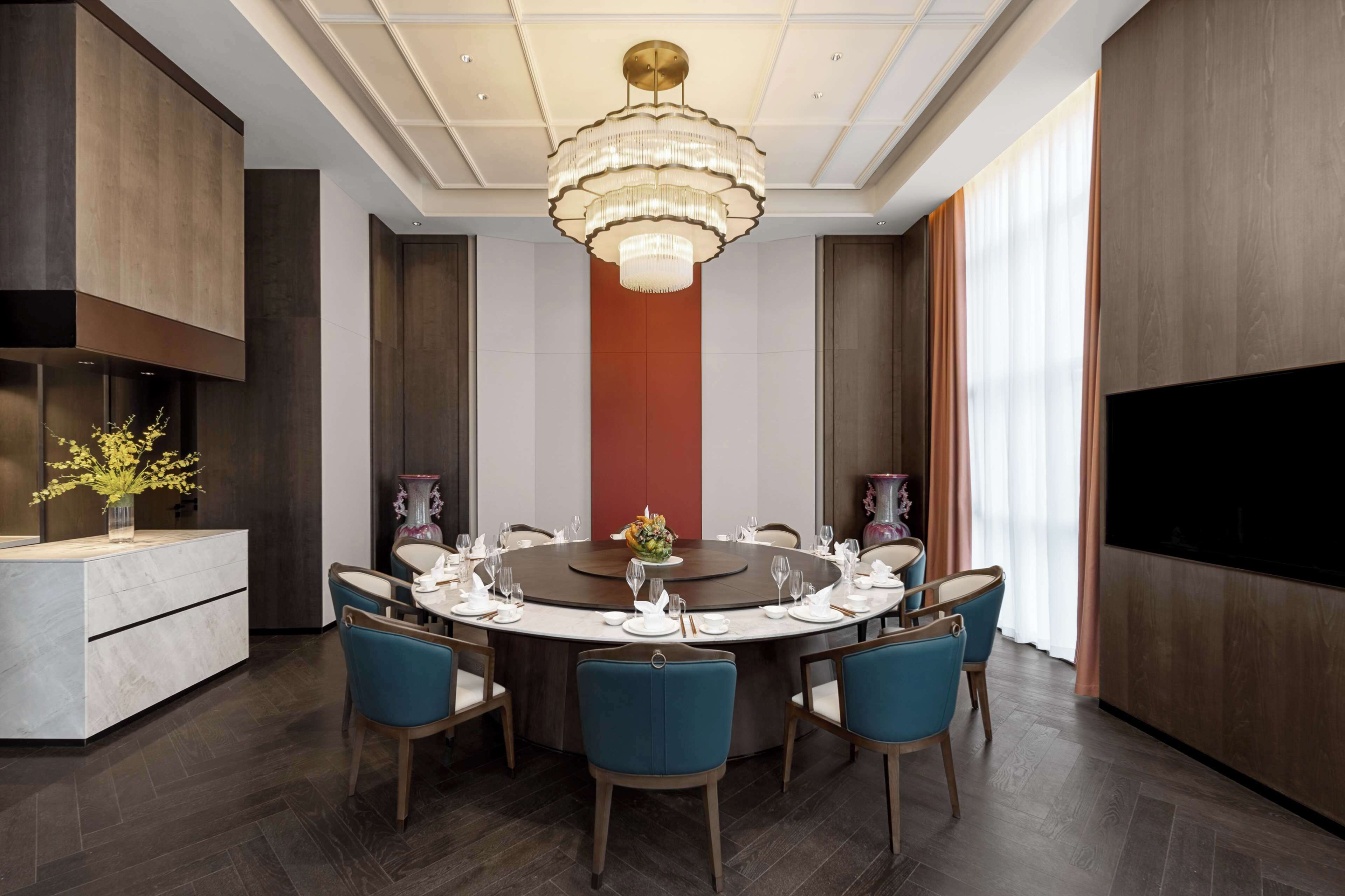 Uma sala de jantar moderna com uma mesa redonda posta para seis pessoas, rodeada por cadeiras estofadas azuis.