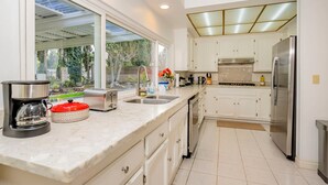 Cozinha moderna com armários brancos, geladeira de aço inoxidável e uma janela grande com vista para um jardim.