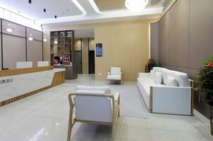 Um saguão de hotel com balcão de recepção, área de estar e uma TV na parede.