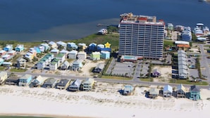 Vista aérea de uma área hoteleira costeira com vários edifícios, incluindo um hotel de grande porte com teto vermelho, e uma praia em primeiro plano.
