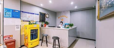 Quarto de hotel com cozinha compacta, máquina de vendas amarela, área de bar e um quadro na parede.