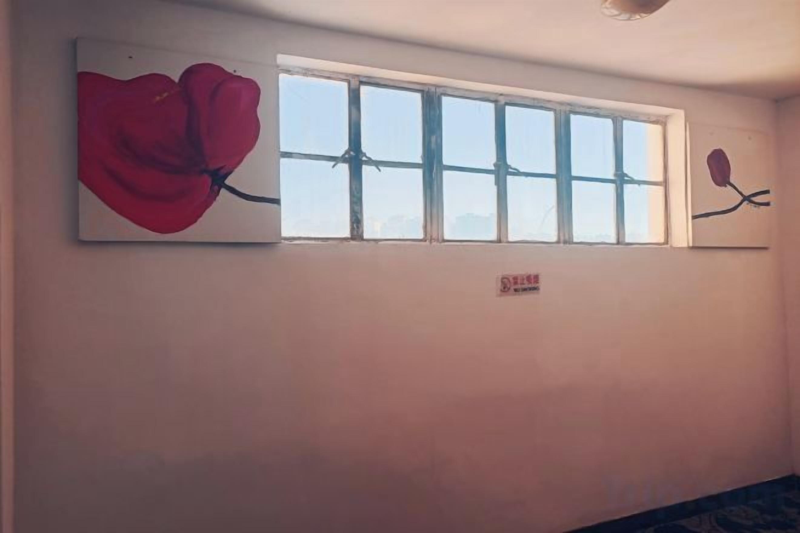 Quarto com janela, pintura de uma flor vermelha e um aviso na parede.