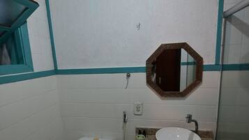 Um banheiro pequeno com vaso sanitário branco, pia com espelho e área de chuveiro.