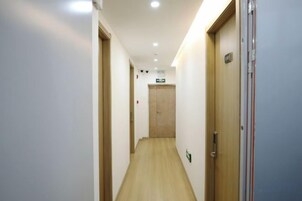 Um corredor estreito com soalho de madeira, portas em ambos os lados e teto com iluminação embutida.