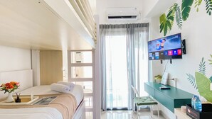 Quarto de hotel com cama, televisão na parede, secretária com cadeira e janela com cortinas.