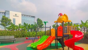 Um parquinho com escorregadores e uma estrutura de escalada, cercado por vegetação e um edifício ao fundo.