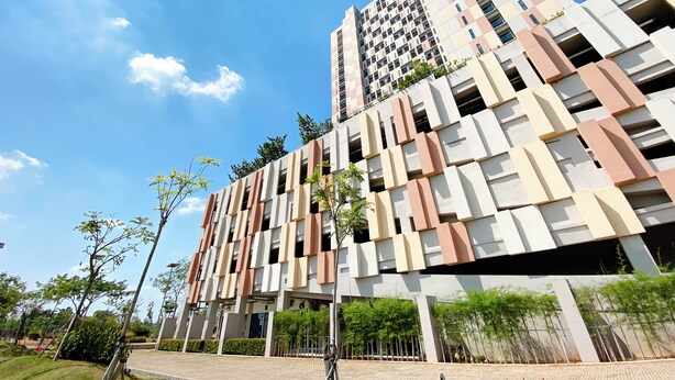 Um edifício alto com design arquitetônico moderno, com várias varandas e uma fachada com painéis bege e rosa.