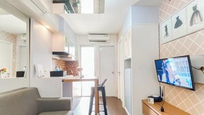 Sala de estar moderna com sofá, televisão na parede e cozinha ao fundo.