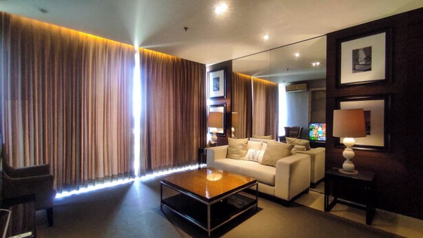 Quarto de hotel moderno com um espelho grande, um sofá, uma mesa de centro e uma televisão.