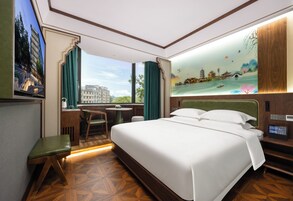 Quarto de hotel com uma cama grande, uma escrivaninha e vista para o horizonte urbano pela janela.