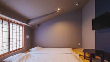 Um quarto com uma cama, uma mesinha, uma televisão e uma janela com divisórias shoji.