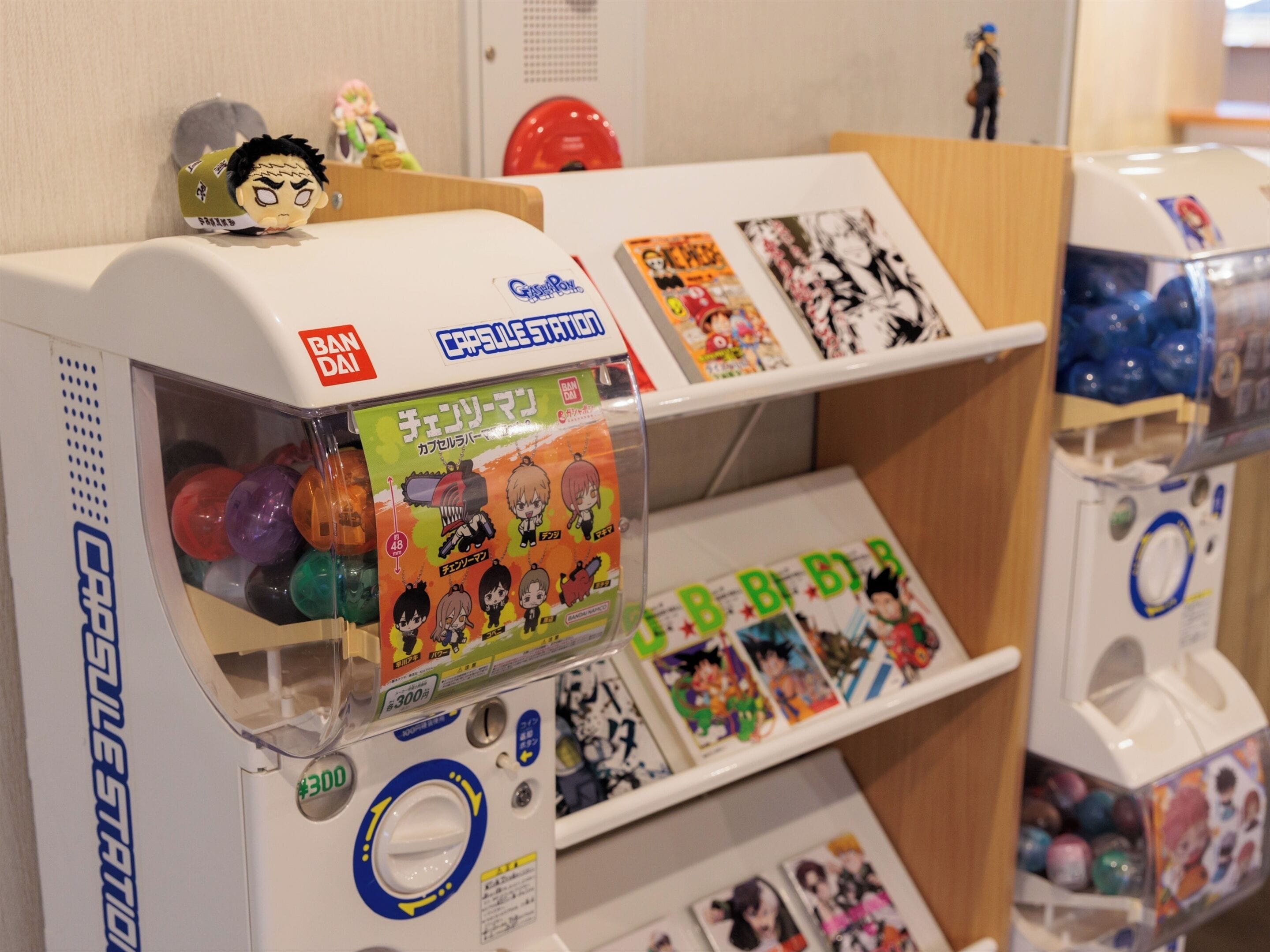 Máquina de vendas com produtos de manga e anime, incluindo pelúcias e DVDs.