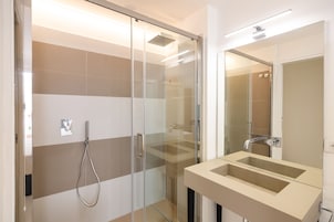 Uma casa de banho moderna com cabine de duche em vidro, lavatório bege com espelho e suporte de toalhas visível.