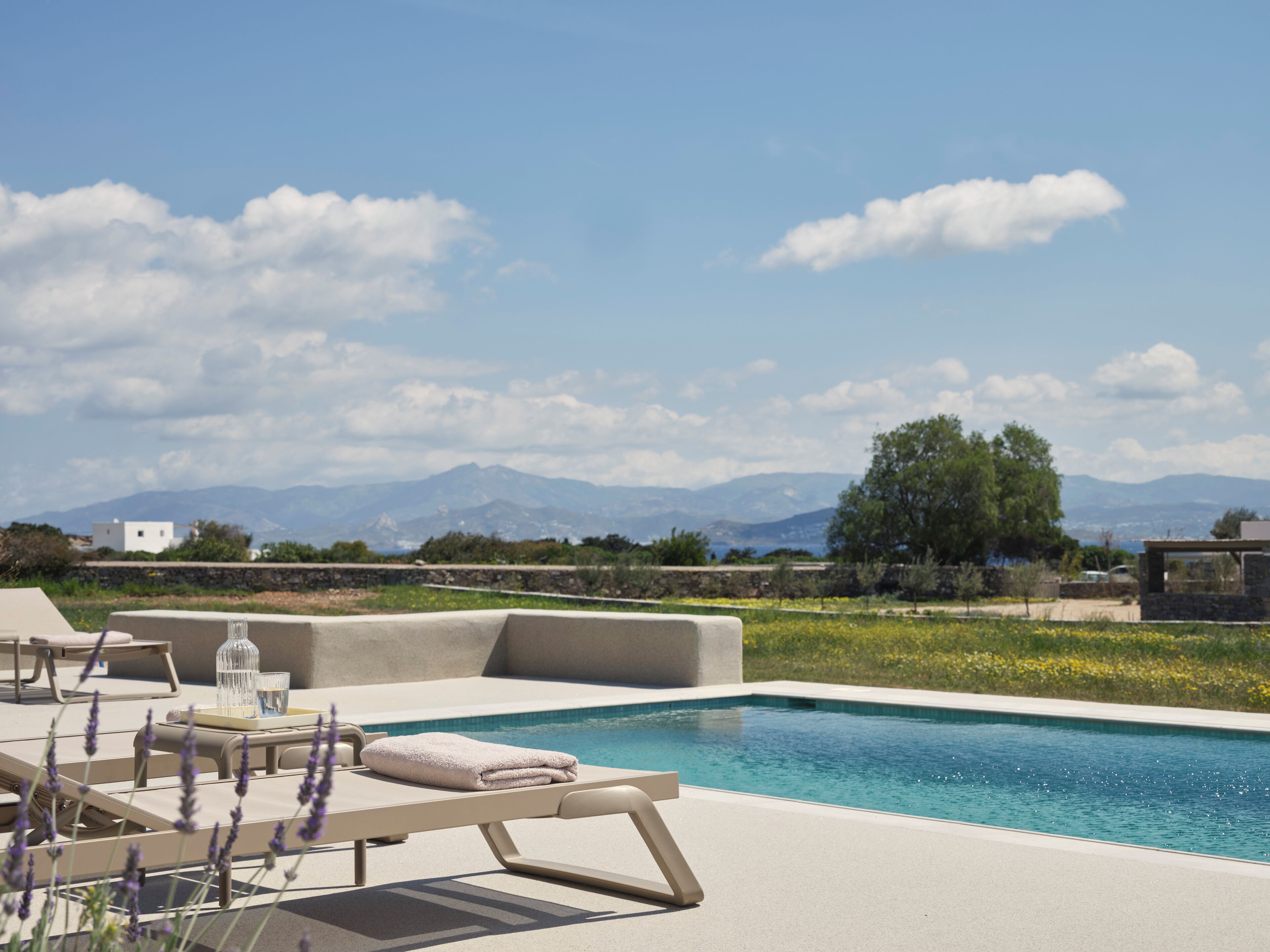Uma área na piscina com espreguiçadeiras, uma mesinha com um copo e um tabuleiro, e vista para montanhas ao fundo.