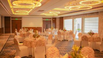 Uma sala de banquetes com mesas redondas, cadeiras brancas e centros de mesa florais.