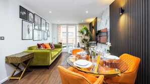 Uma sala de estar moderna com um sofá verde, cadeiras laranja e uma mesa de jantar de vidro para quatro pessoas.