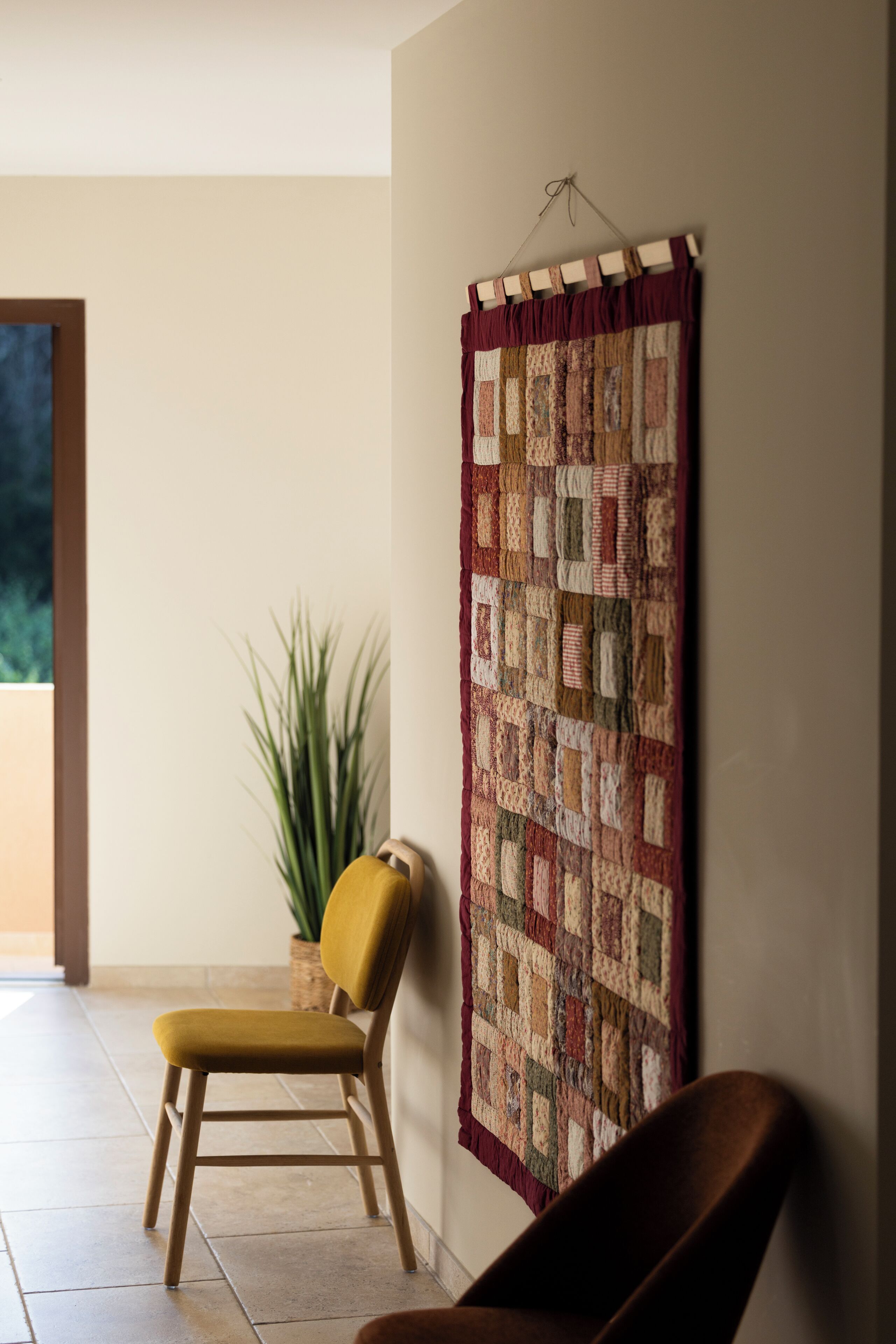 Quarto com cadeira de madeira, colcha pendurada e planta em vaso.