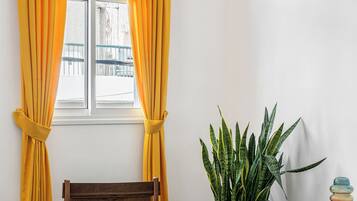 Um quarto com uma cadeira de madeira, uma mesa redonda, um vaso de planta e uma janela com cortinas amarelas.