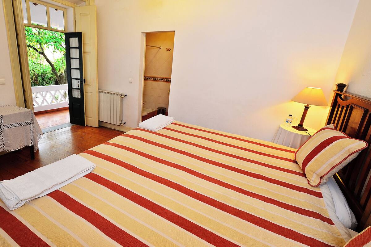 Quarto de hotel com uma cama, uma mesinha de cabeceira com abajur e vista para o exterior.