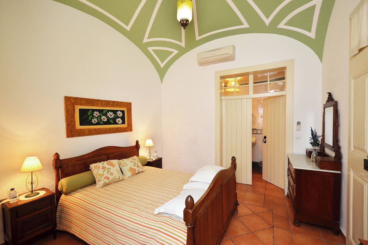 Um quarto com uma cama, mesas de cabeceira, cômoda e um espelho.