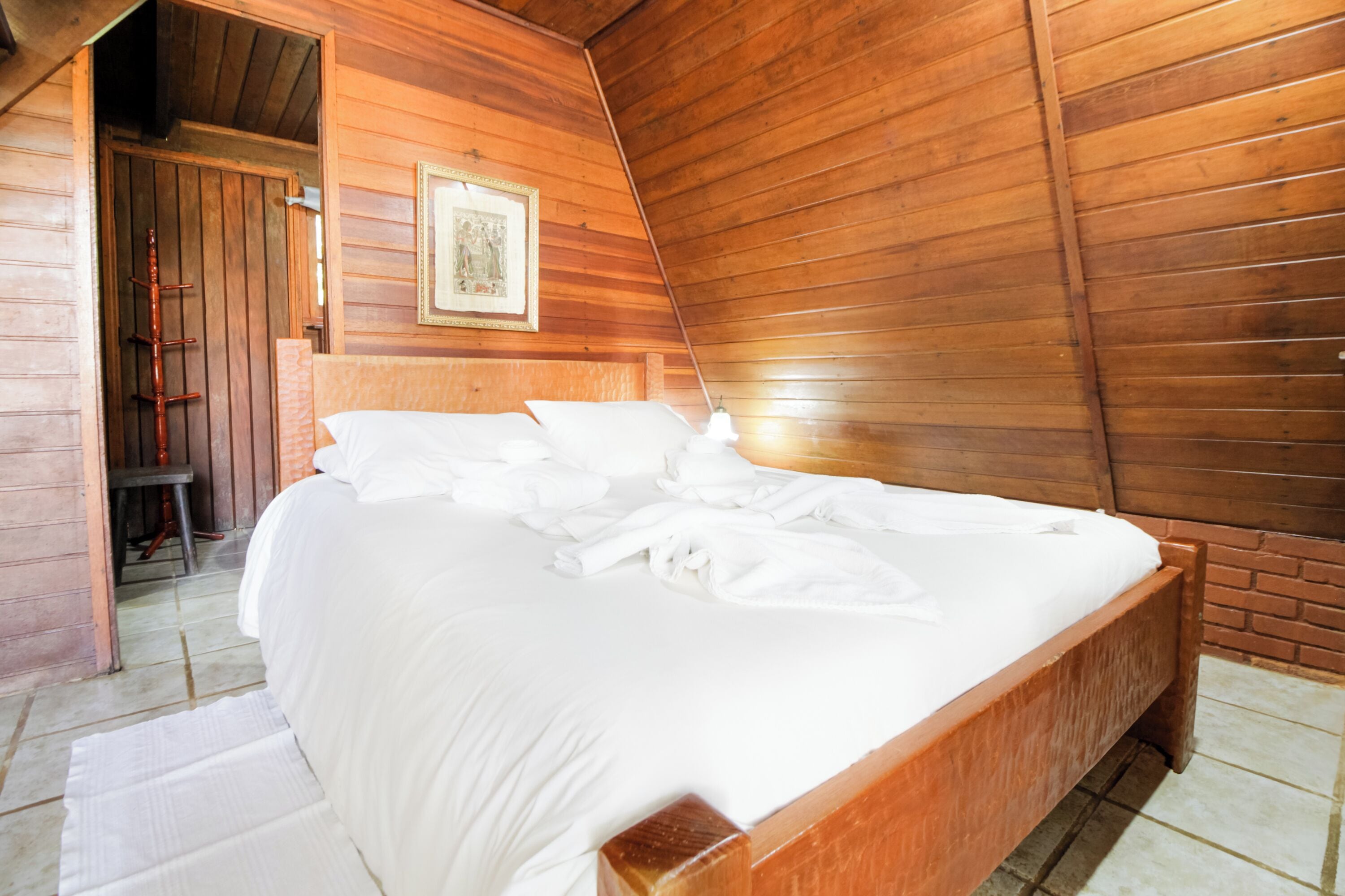 Quarto com painéis de madeira, uma cama grande, um quadro na parede e uma cadeira de madeira perto da porta.