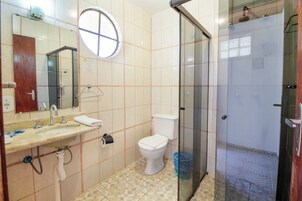 Casa de banho com lavatório, sanita e cabine de duche com parede de vidro.