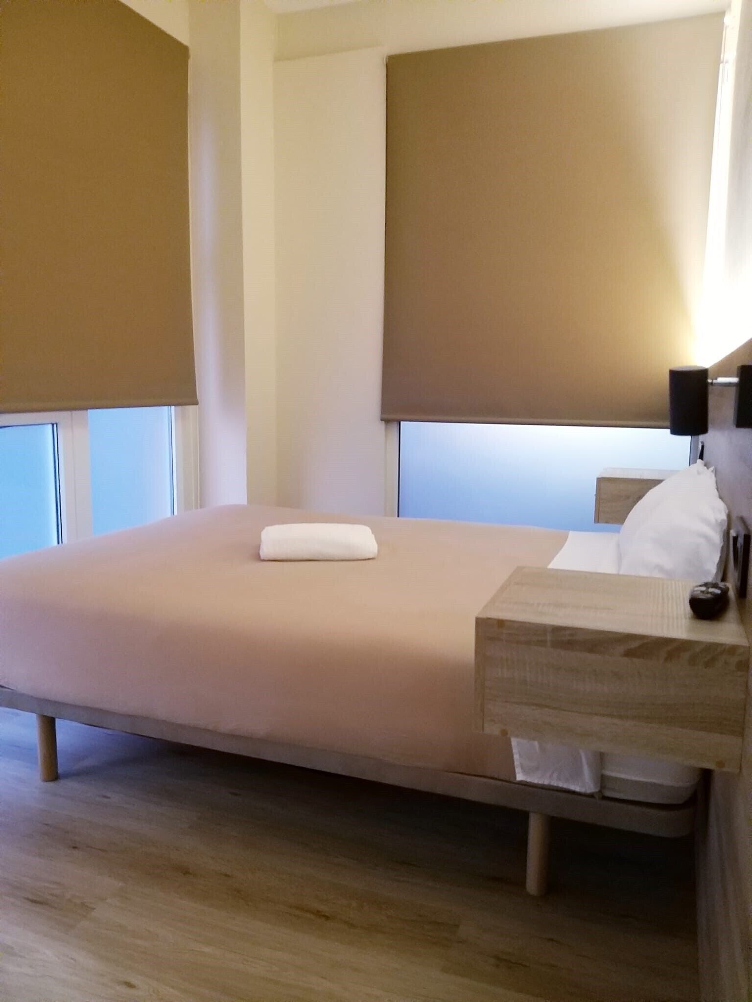 Quarto de hotel com cama, mesa de cabeceira e janela com persianas.