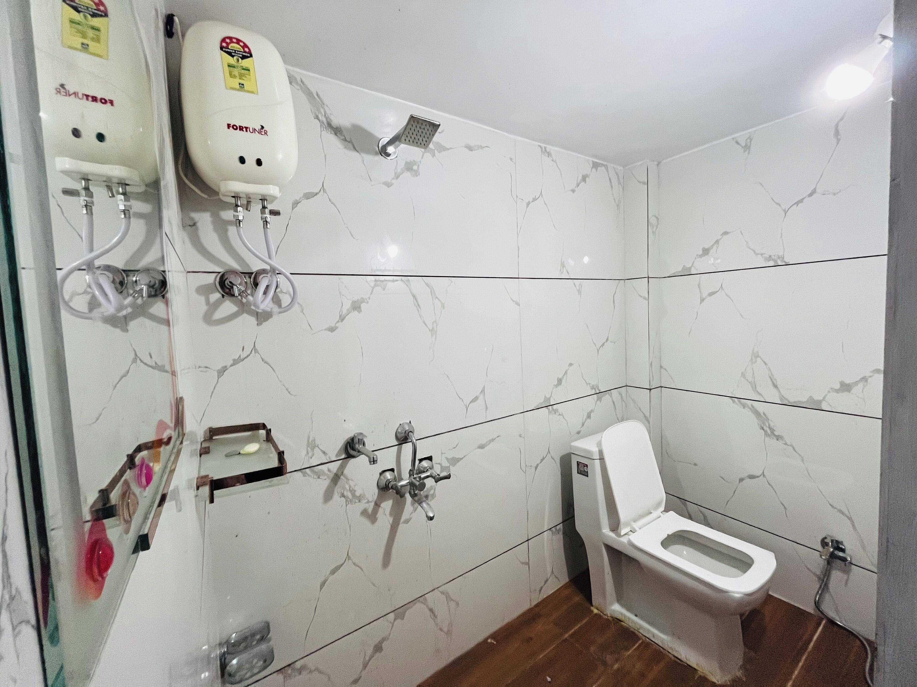 Casa de banho com azulejos de mármore branco, sanita, secador de mãos e dispensador de sabonete.